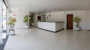 Uma área de recepção limpa e moderna, com balcão, plantas em vasos e um relógio na parede.