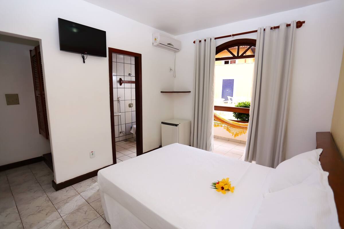 Quarto de hotel com cama, televisão, ar condicionado, banheiro e vista para o exterior.