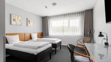 Quarto de hotel com duas camas, uma escrivaninha, uma cadeira, uma televisão e obras de arte na parede.