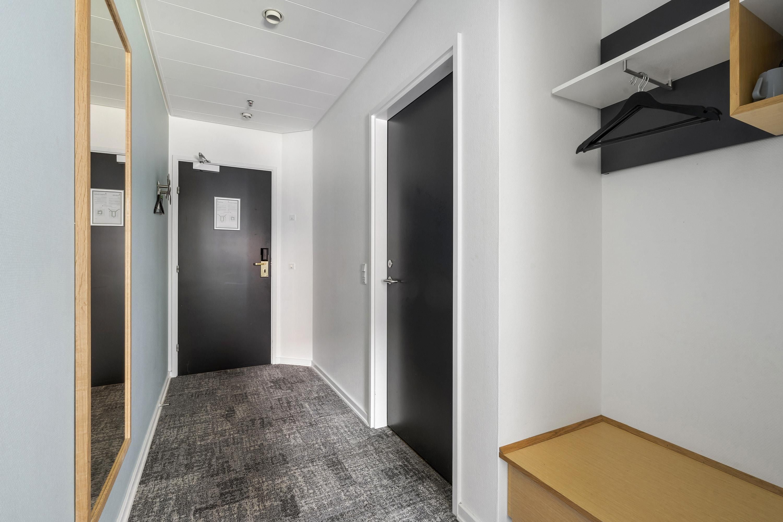 Um corredor com espelho, porta, cabideiro e uma pequena mesa de madeira.