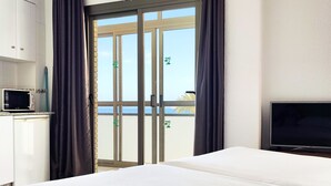 Quarto de hotel com uma cama, televisão, micro-ondas e porta de vidro deslizante para uma varanda.