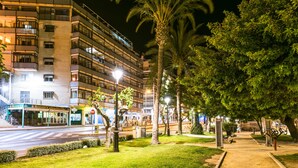 Um hotel com vários andares e varandas, rua bem iluminada e palmeiras.