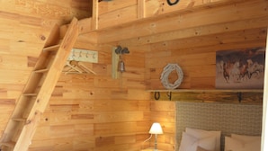 Quarto de cabana de madeira aconchegante com beliche, mesa de cabeceira pequena, luminária e decoração rústica na parede.