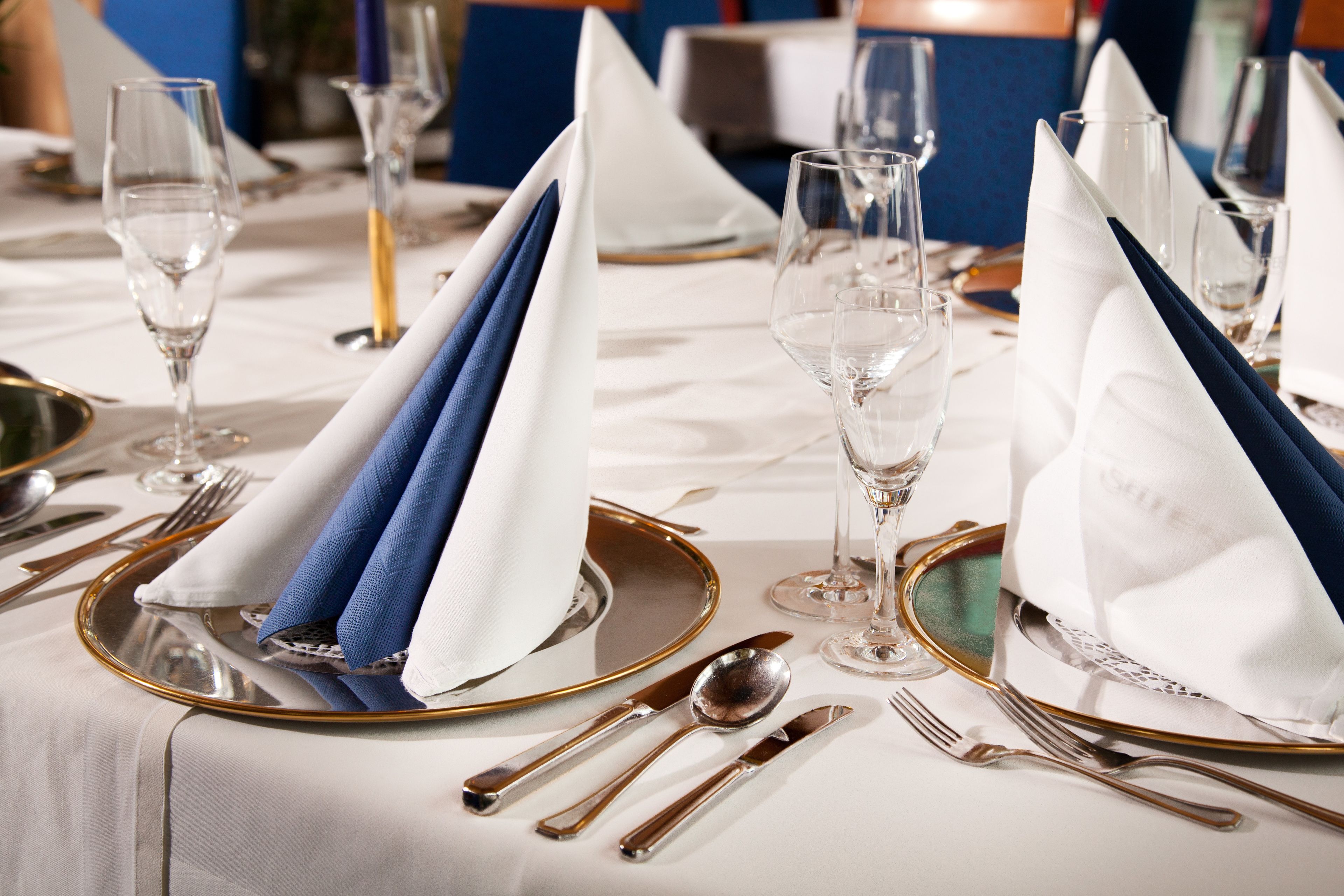 Uma mesa posta com guardanapos brancos, guardanapos azuis e pratos com detalhes dourados.