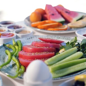 Uma mesa com diversos alimentos, incluindo tomates fatiados, pepinos, pimentões verdes e melancia.