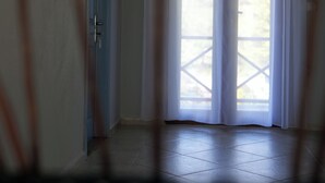 Um quarto com porta, janela com cortinas e piso de azulejos.