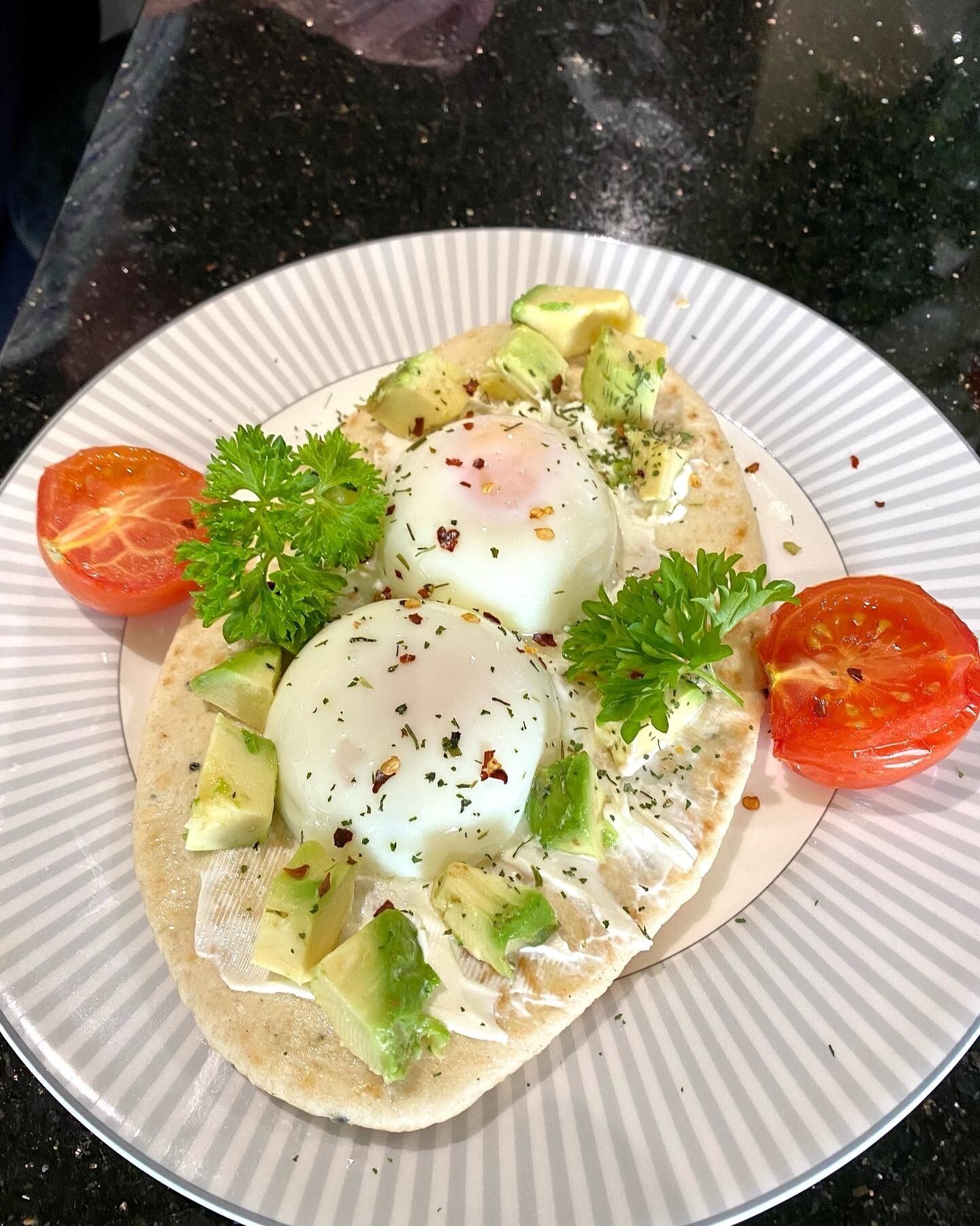 Um prato com pão sírio coberto com fatias de abacate, um ovo pochê e finalizado com ervas e tomates.