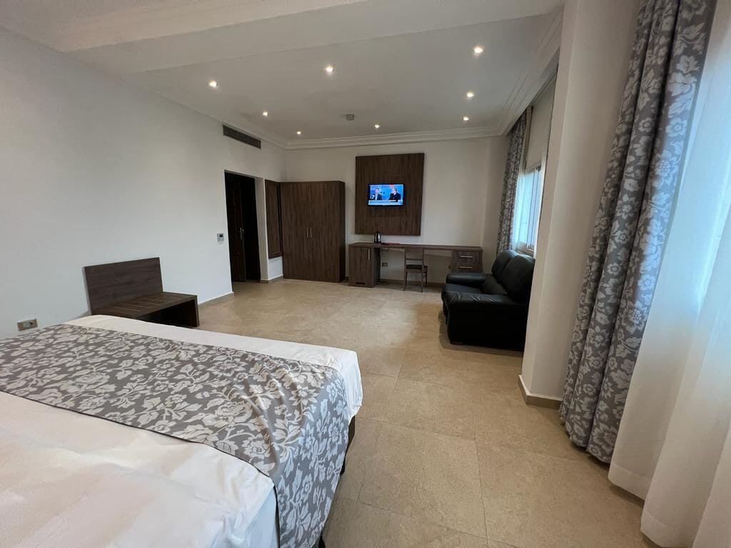 Quarto de hotel com cama, escrivaninha, televisão e área de estar.