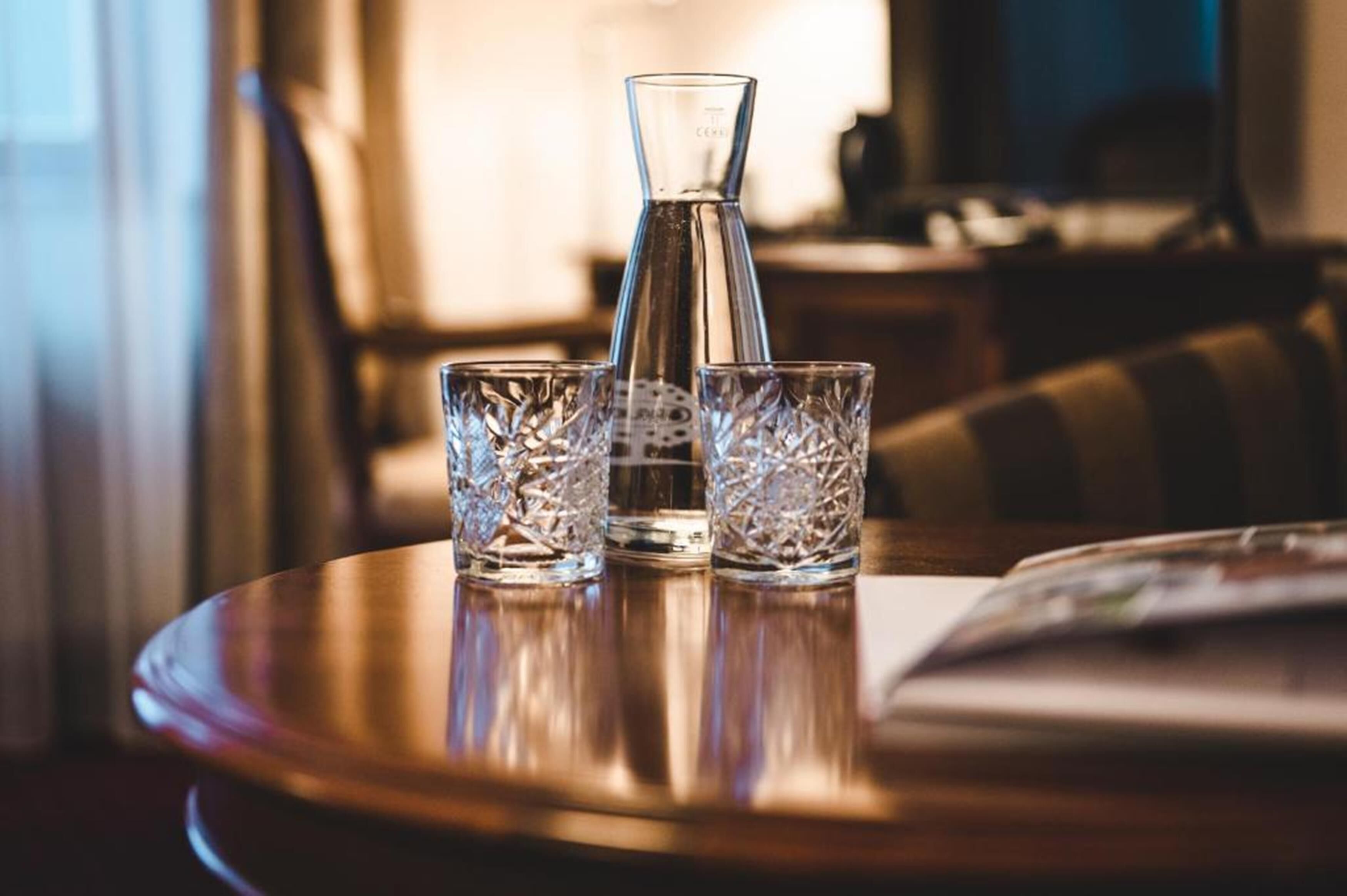 Uma mesa com três copos de cristal e uma garrafa de vidro transparente.