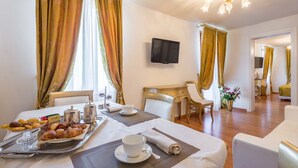 Quarto de hotel com área de jantar, televisão fixada na parede, escrivaninha e uma cadeira.