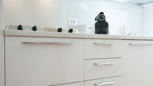 Uma cozinha com armários brancos, bancada e cafeteira.