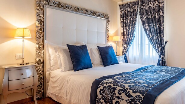Cama bem arrumada com cabeceira estofada, duas luminárias de cabeceira e colcha estampada.