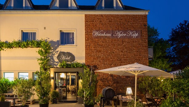 A building with a sign reading "Weinhaus Fischer Kapp" and outdoor seating with umbrellas.