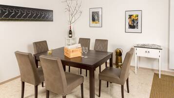 Uma sala de jantar com uma mesa de madeira escura, seis cadeiras, um vaso com galhos e quadros nas paredes.