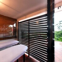 Um quarto com mesa de massagem, parede de madeira e janela com persianas.