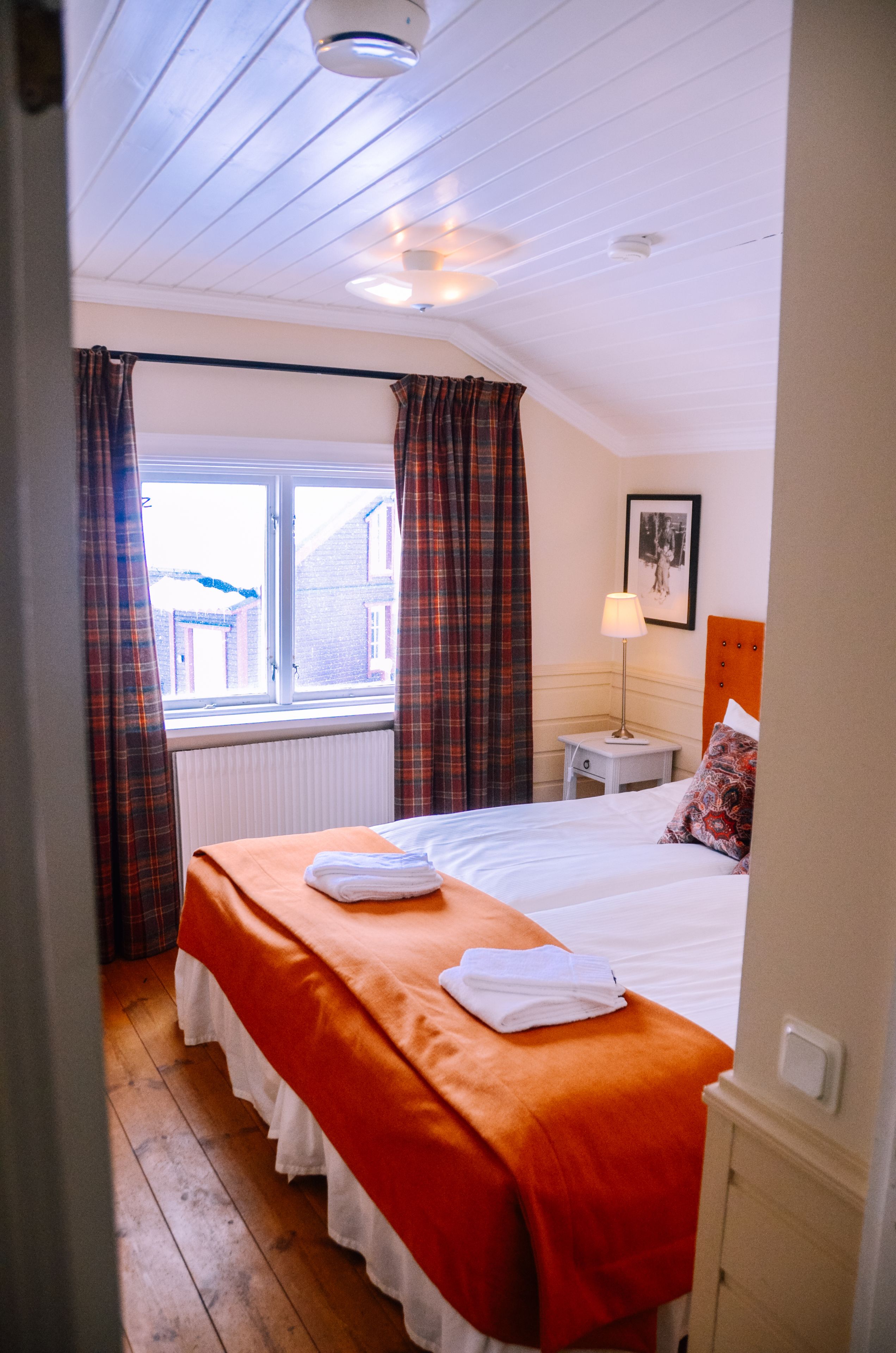 Quarto com cama, janela com cortinas, mesa de cabeceira com abajur e cabeceira.