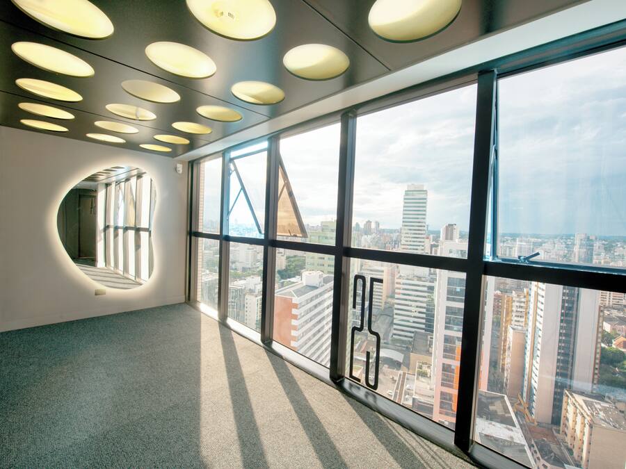 Interior moderno com grandes janelas, detalhe de parede curva e vista para a cidade.
