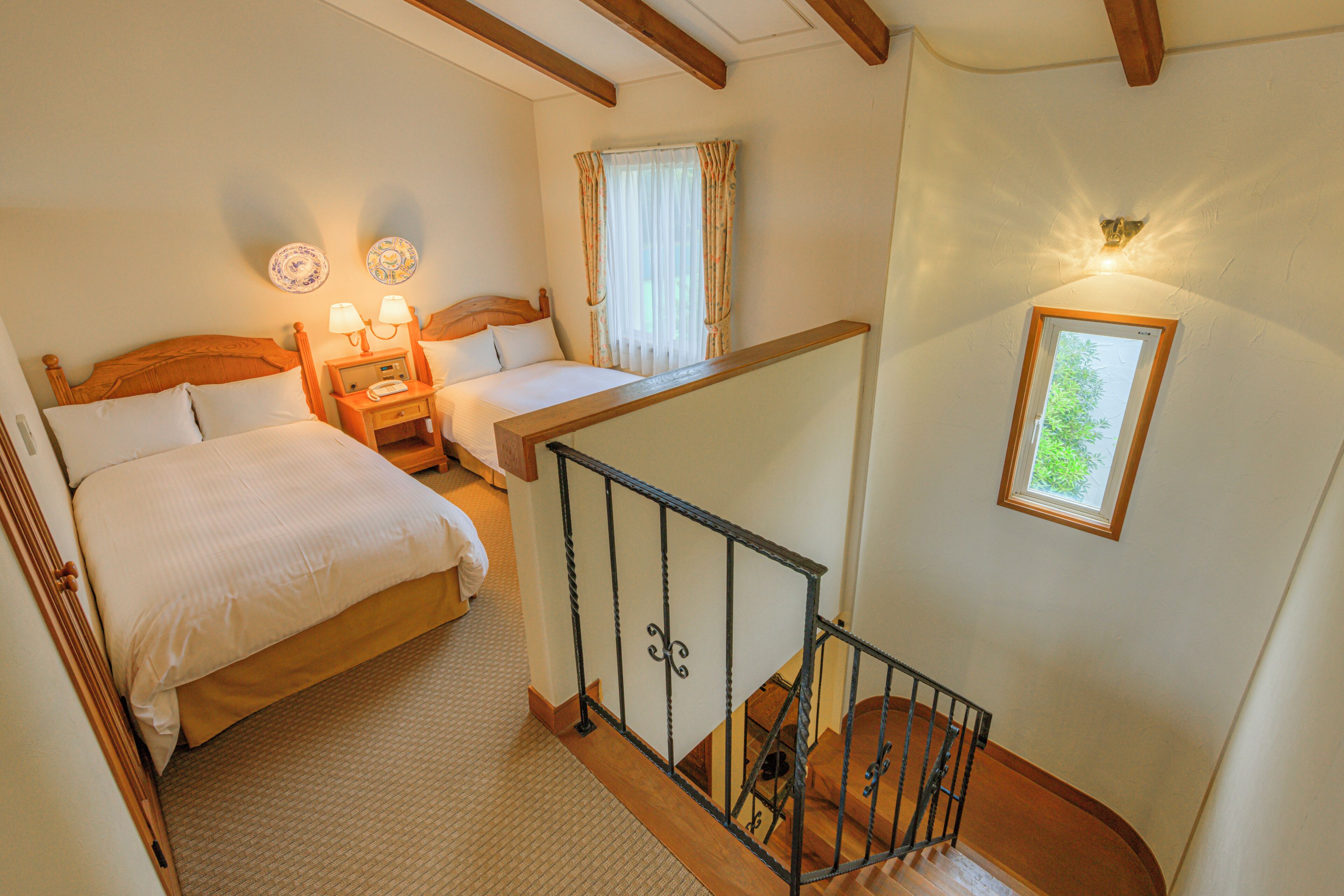Quarto com duas camas, mesa de cabeceira com luminárias, janela com cortinas e escada com corrimão.