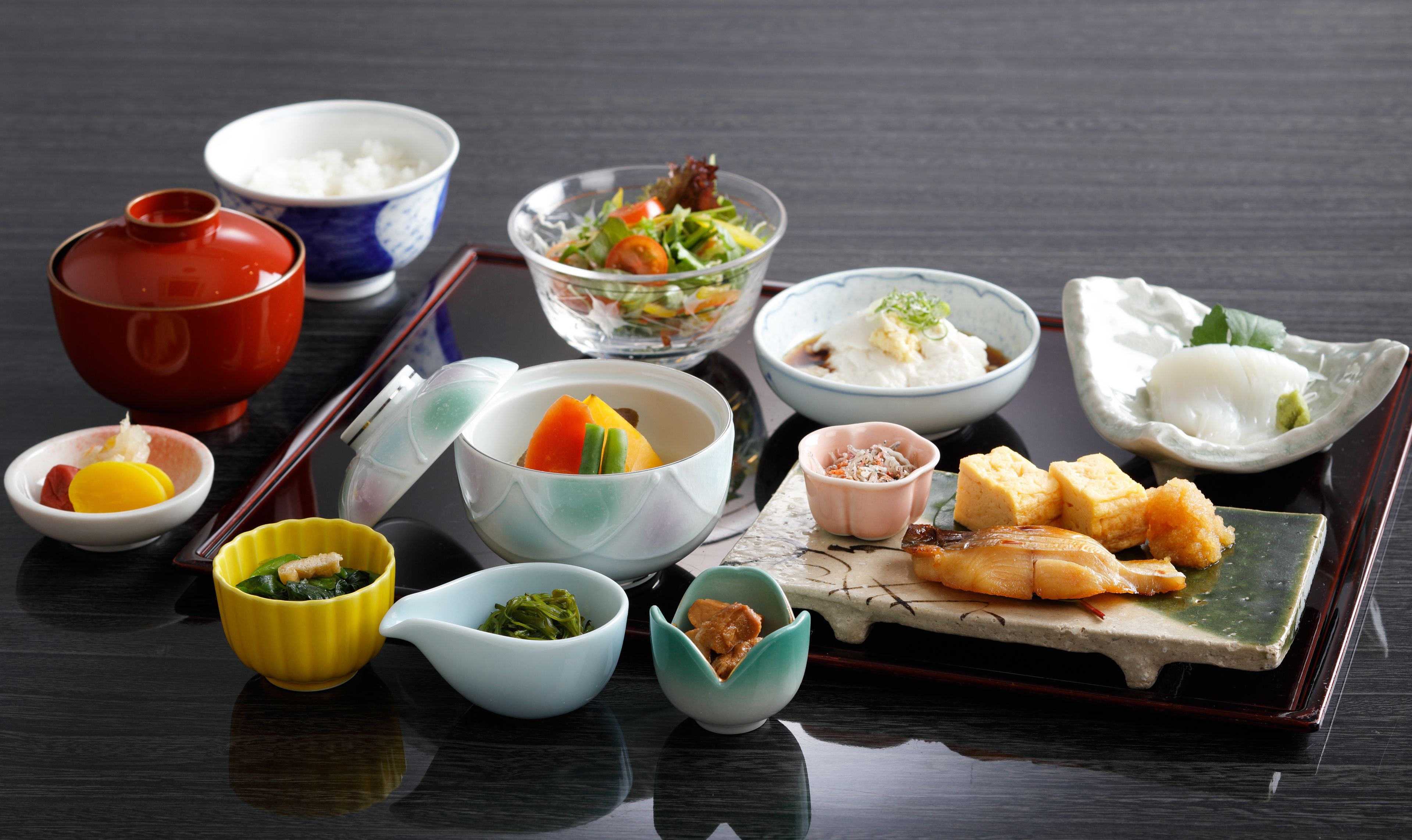 Diversos pratos da culinária japonesa dispostos numa bandeja preta.
