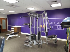 Uma academia com equipamentos de exercício, um banco e uma parede com o texto "100 AHEAD FLEXABLE".