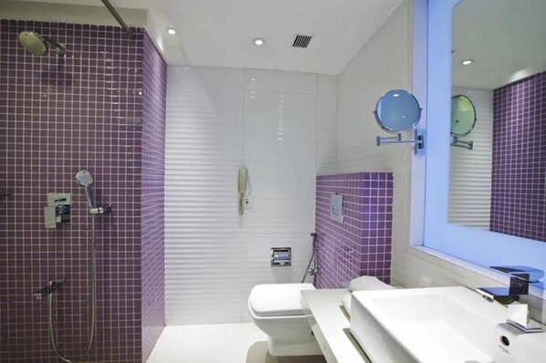 Um banheiro com paredes azulejadas em roxo, vaso sanitário branco, pia com espelho e chuveiro com chuveiro manual.