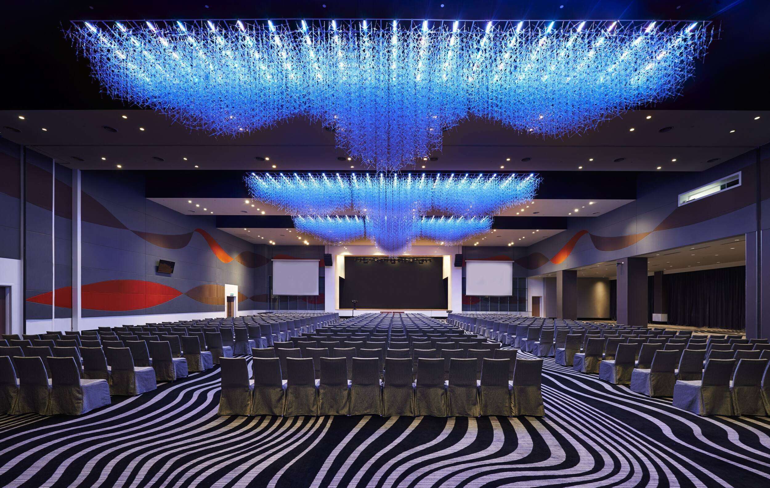A conference room with rows of chairs, a large screen, and a ceiling light installation.