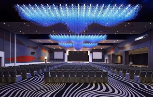 Uma sala de conferências com fileiras de cadeiras, uma tela grande e uma instalação de iluminação no teto.