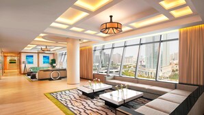 Um hall de hotel moderno com uma ampla área de estar, balcão de recepção e vista para a cidade através de grandes janelas.