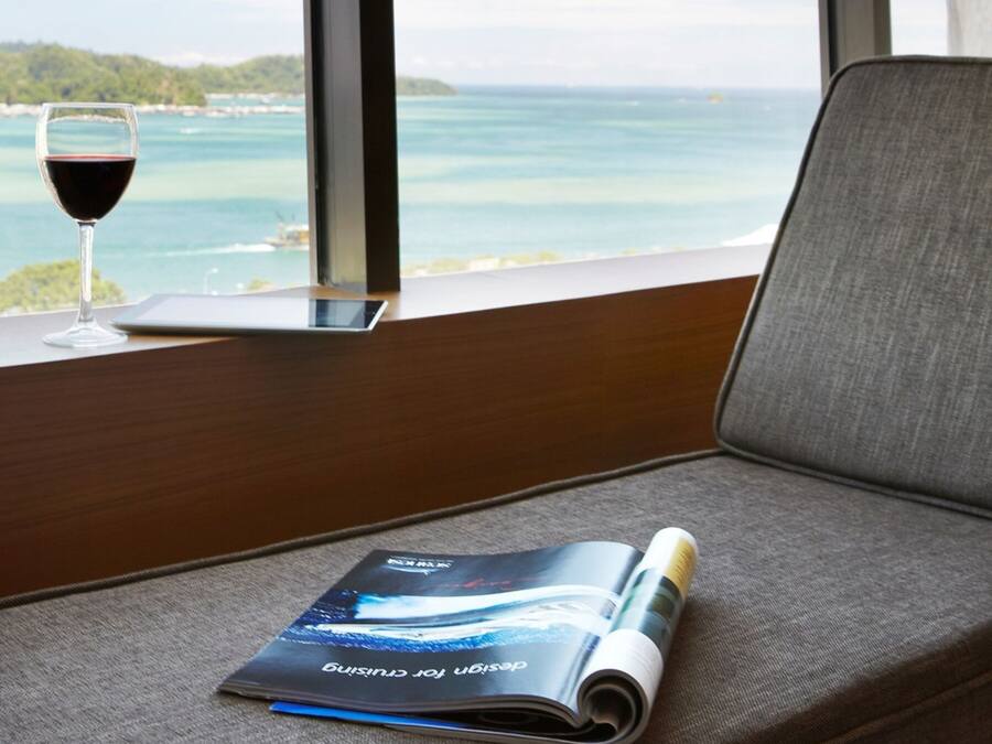 Vista da janela com um copo de vinho tinto e uma revista em um assento acolchoado.