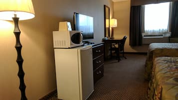 Quarto de hotel com cama, escrivaninha e cadeira, televisão, micro-ondas, luminária e janela com cortinas.
