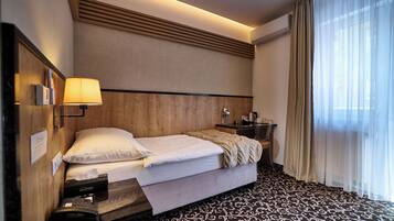 Quarto de hotel com cama, abajur, telefone e escrivaninha com luminária.