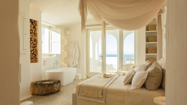 Quarto com uma cama grande, uma banheira e vista para o mar.