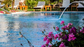 Piscina com espreguiçadeiras e guarda-sóis, rodeada por vegetação e flores.