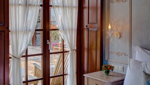 Quarto com porta de madeira, cortinas brancas, uma pequena mesa com um vaso de flores e um aplique de parede.