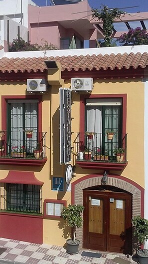 Um edifício amarelo com telhado vermelho, duas unidades de ar condicionado e uma placa com a inscrição 