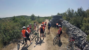 Ciclistas em um caminho de terra com uma parede de pedra de um lado e vegetação do outro.