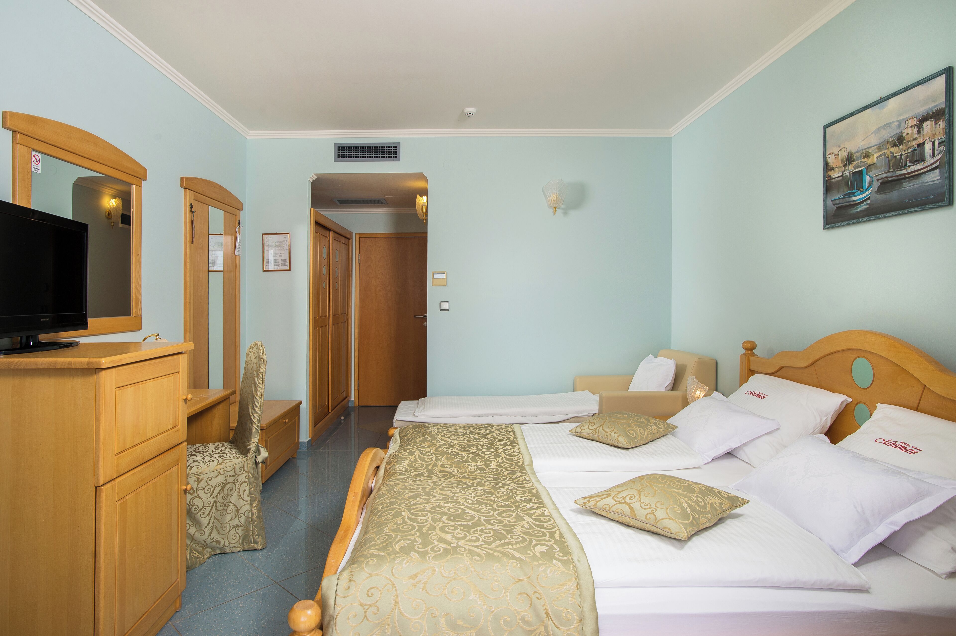 Quarto de hotel com cama, televisão, cómoda de madeira e um quadro na parede.