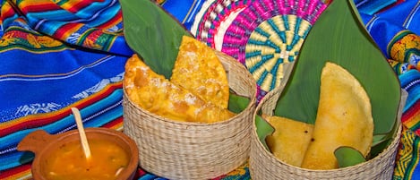Duas cestas de tecido com alimentos, uma tigela pequena de sopa e um tecido colorido.