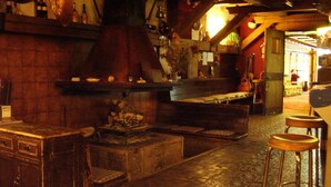Uma área de bar rústica com móveis de madeira, balcão e um sinal indicando a localização dos sanitários.