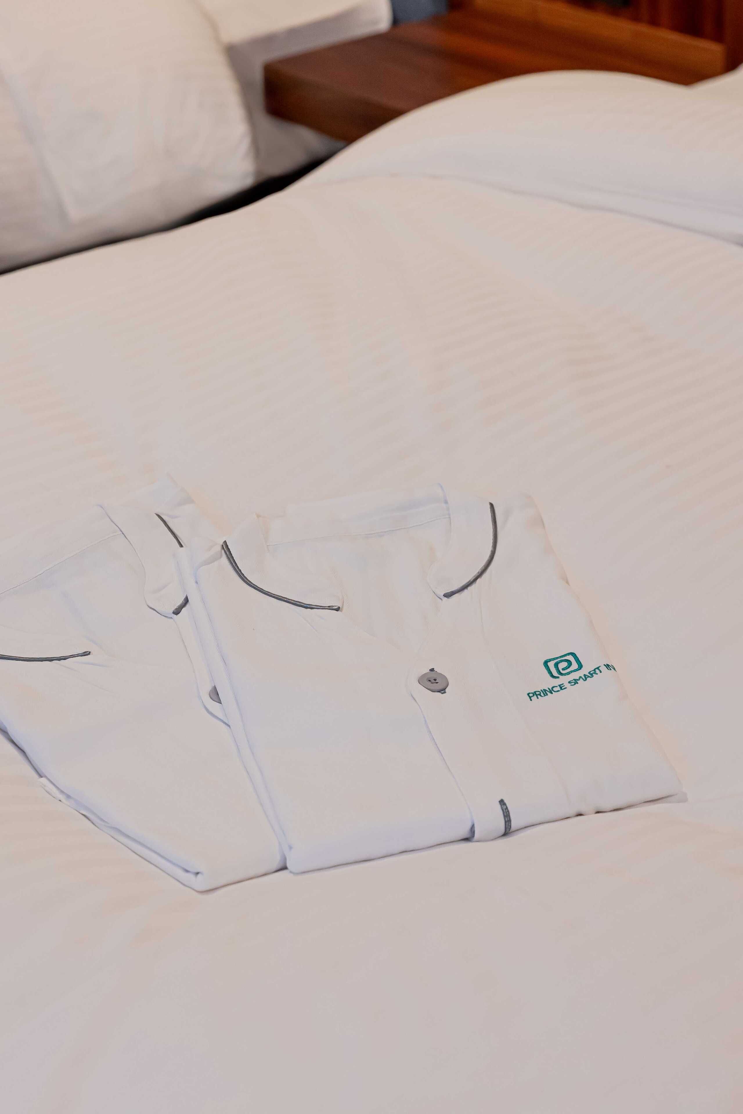 Uma cama bem arrumada com roupa de cama branca e uma camisa branca dobrada com um logotipo.
