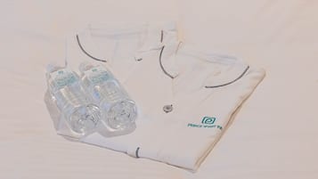 Uma camisa polo branca, bem dobrada, com um logotipo e duas garrafas de plástico transparentes, com etiquetas.