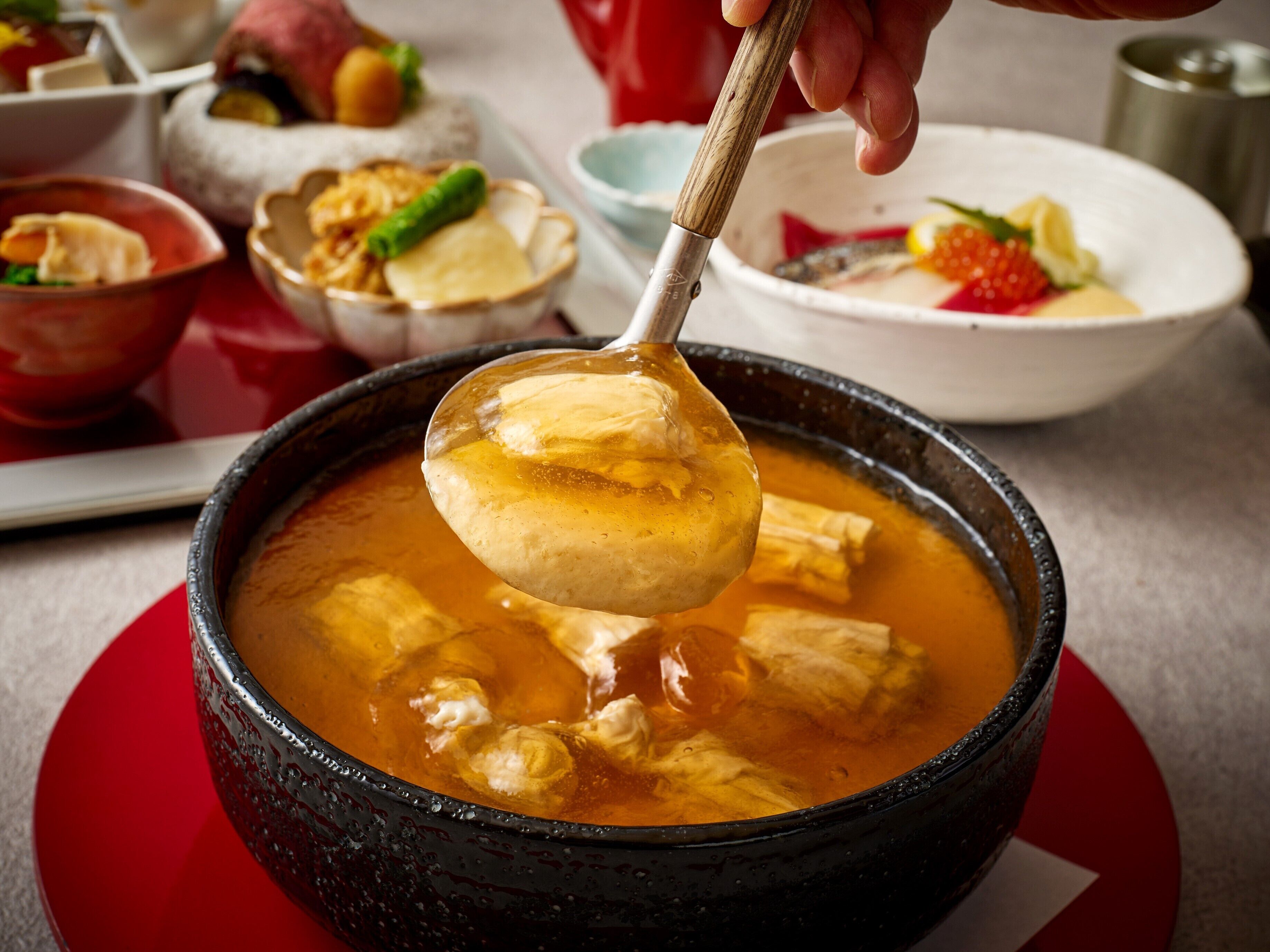 Uma tigela de sopa com uma concha, cercada por diversos pratos sobre uma mesa.