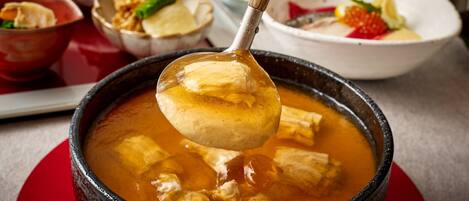Uma tigela de sopa com uma concha, cercada por diversos pratos sobre uma mesa.