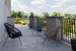 Uma varanda com três cadeiras, piso de concreto e vista para áreas verdes e edifícios.