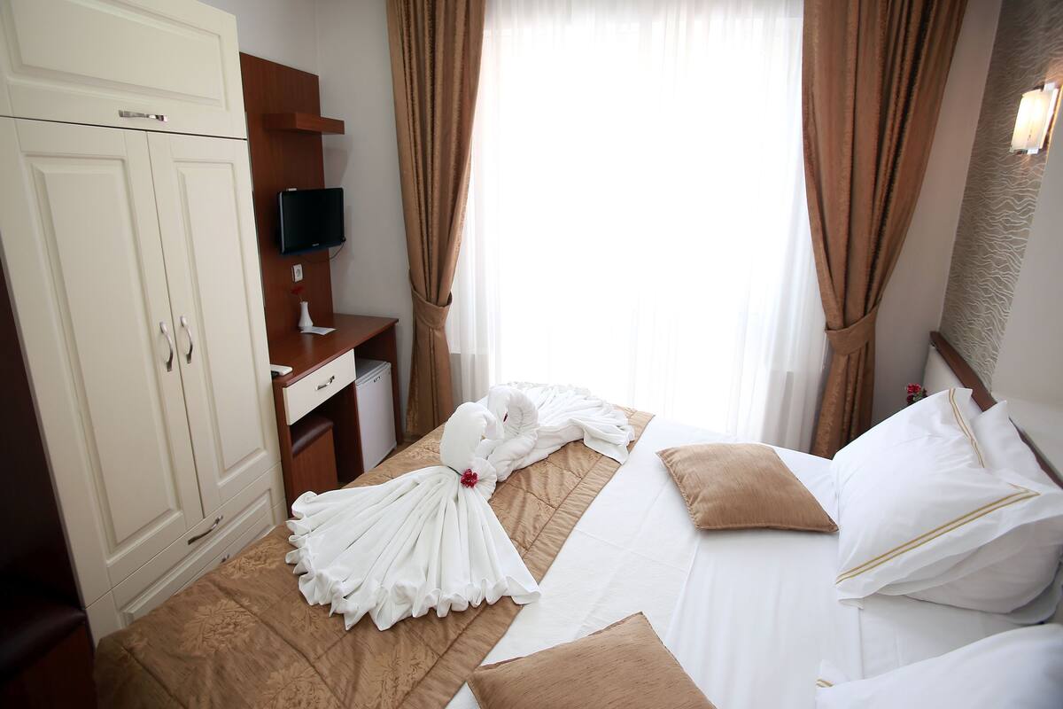 Quarto de hotel com cama, secretária, televisão e guarda-roupa.