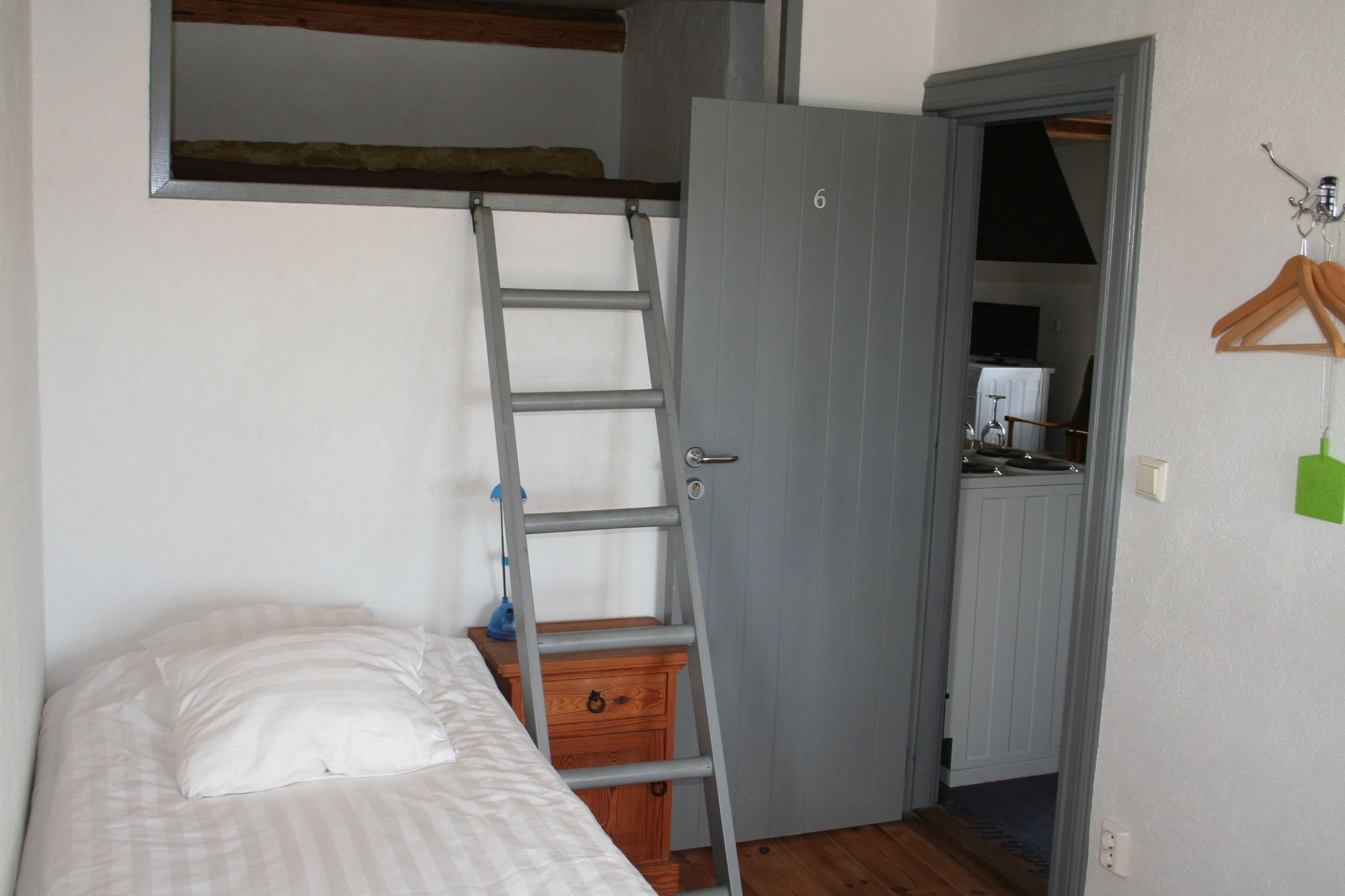 Quarto com beliche, cómoda de madeira e escada para um espaço de dormir elevado.