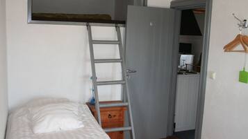 Quarto com beliche, cómoda de madeira e escada para um espaço de dormir elevado.