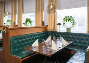 Uma cabine nos cantos com mesa de madeira posta para refeição, assentos estofados em verde e vista da rua através de grandes janelas.