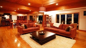 Uma sala de estar espaçosa com piso de madeira, dois sofás vermelhos, uma mesa de centro e um lustre.
