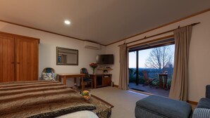 Quarto com uma cama grande, uma escrivaninha com televisão e uma varanda com área de estar.